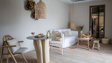 Uma sala de estar moderna com uma mesa redonda, duas cadeiras, um sofá e uma pequena mesa lateral com frutas.