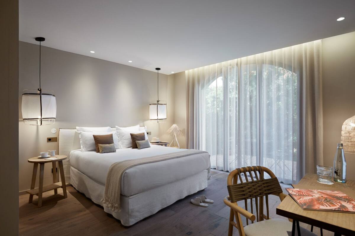 Quarto moderno com uma cama grande, mesas de cabeceira, uma cadeira e uma mesa com abajur.