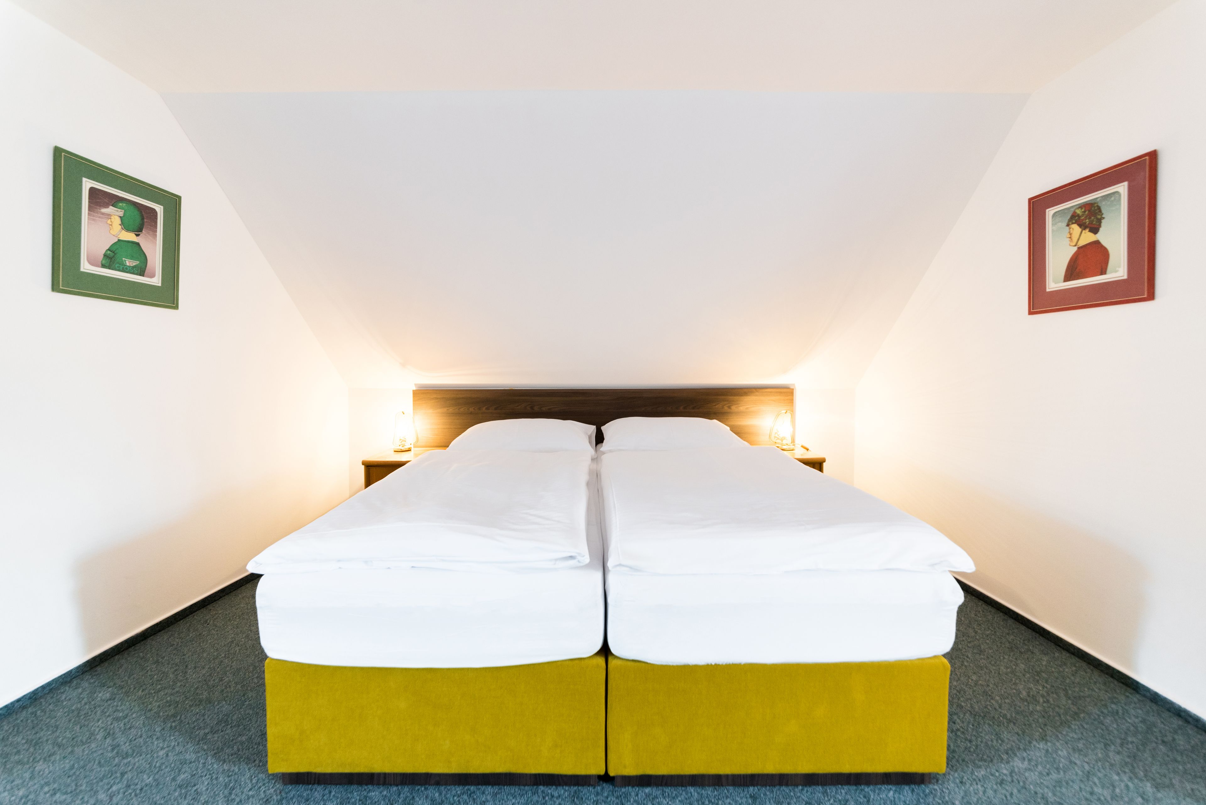 Quarto com uma cama posicionada sob um teto inclinado, com duas luminárias fixadas nas paredes.