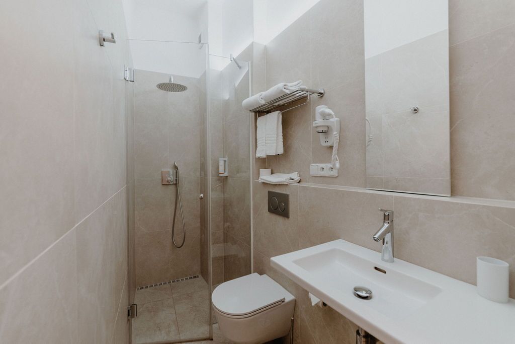 Uma casa de banho moderna com chuveiro em cabine de vidro, sanita, lavatório e porta-toalhas.