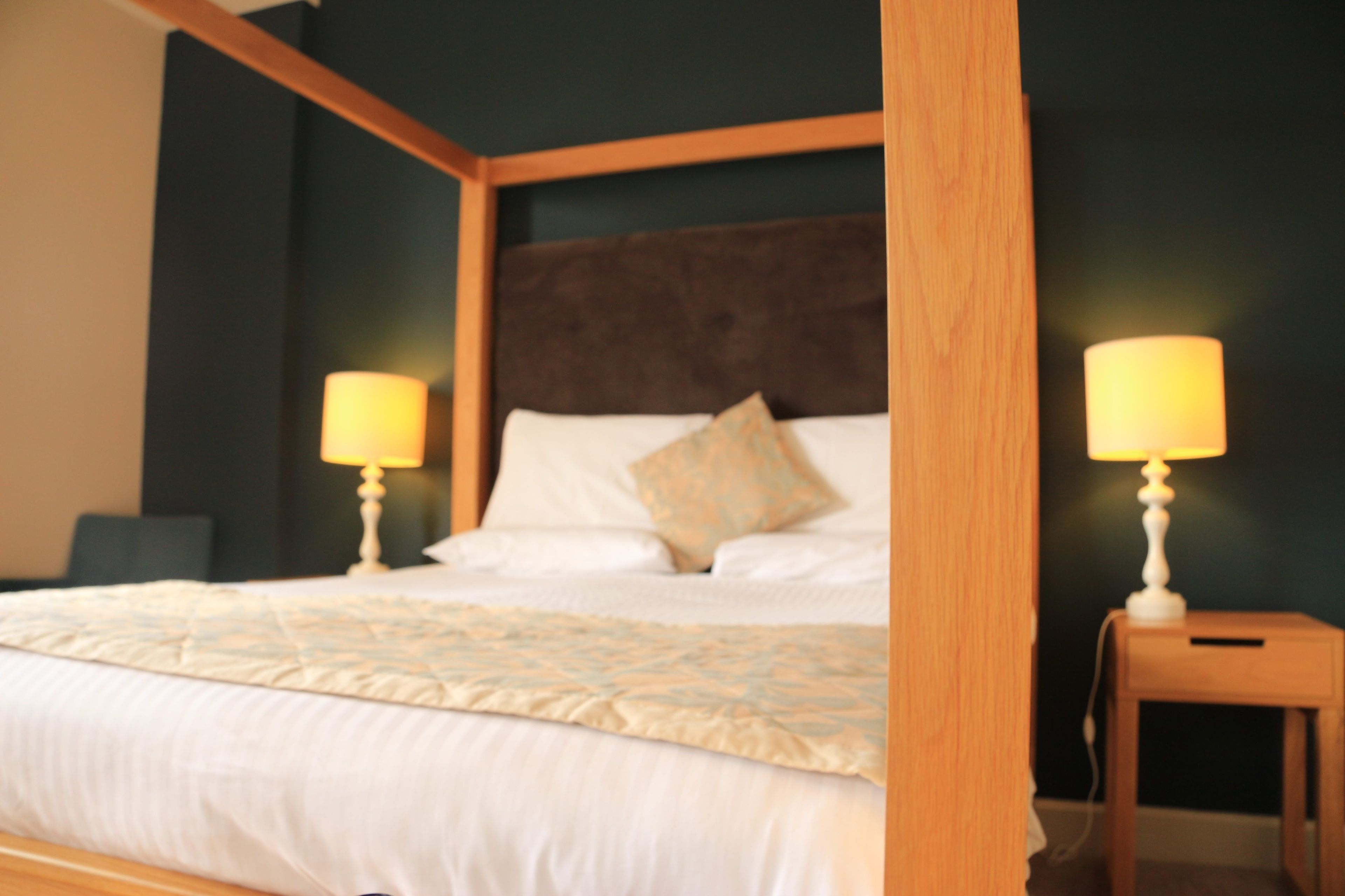 Cama bem arrumada com cabeceira de madeira, duas luminárias de cabeceira e uma pequena mesa de cabeceira de madeira.