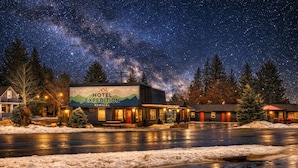 Um hotel chamado "Hotel Expedition Montana" com um céu estrelado, chão coberto de neve e um estacionamento.