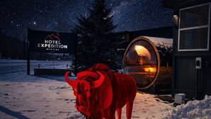 Paisagem coberta de neve com uma placa indicando 'Hotel Expedition Montana' e uma escultura de um touro vermelho.