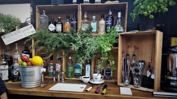 Uma área de bar com diversas garrafas de gin e outras bebidas, um balde de frutas e uma xícara de café.