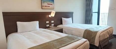 Quarto de hotel com duas camas, uma mesa de cabeceira, um quadro na parede e uma janela com cortinas.