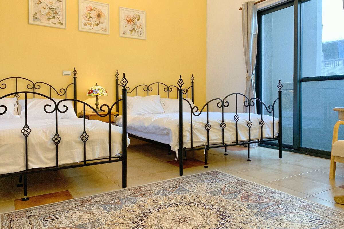 Quarto com duas camas, uma janela grande e um tapete estampado.