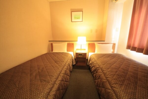 Quarto de hotel com duas camas de solteiro, uma mesa de cabeceira com abajur e um quadro pendurado na parede.