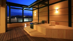 Um spa moderno com piso de madeira, uma banheira de hidromassagem e vista para a cidade ao entardecer.