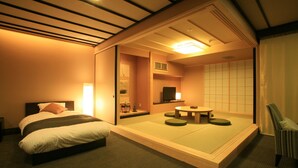 Quarto de hotel com cama, uma pequena mesa, uma cadeira, televisão e área com tatame tradicional japonês.