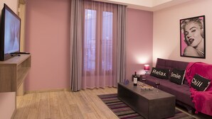 Uma sala de estar moderna com televisão, um sofá com almofadas decorativas, uma garrafa de vinho e um quadro na parede.