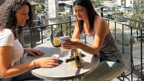 Duas pessoas sentadas numa mesa redonda ao ar livre, com vista para a cidade ao fundo.
