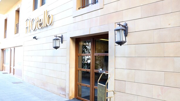 Entrada de um hotel com uma placa indicando 'Hotel', uma porta de vidro e um portão de metal.