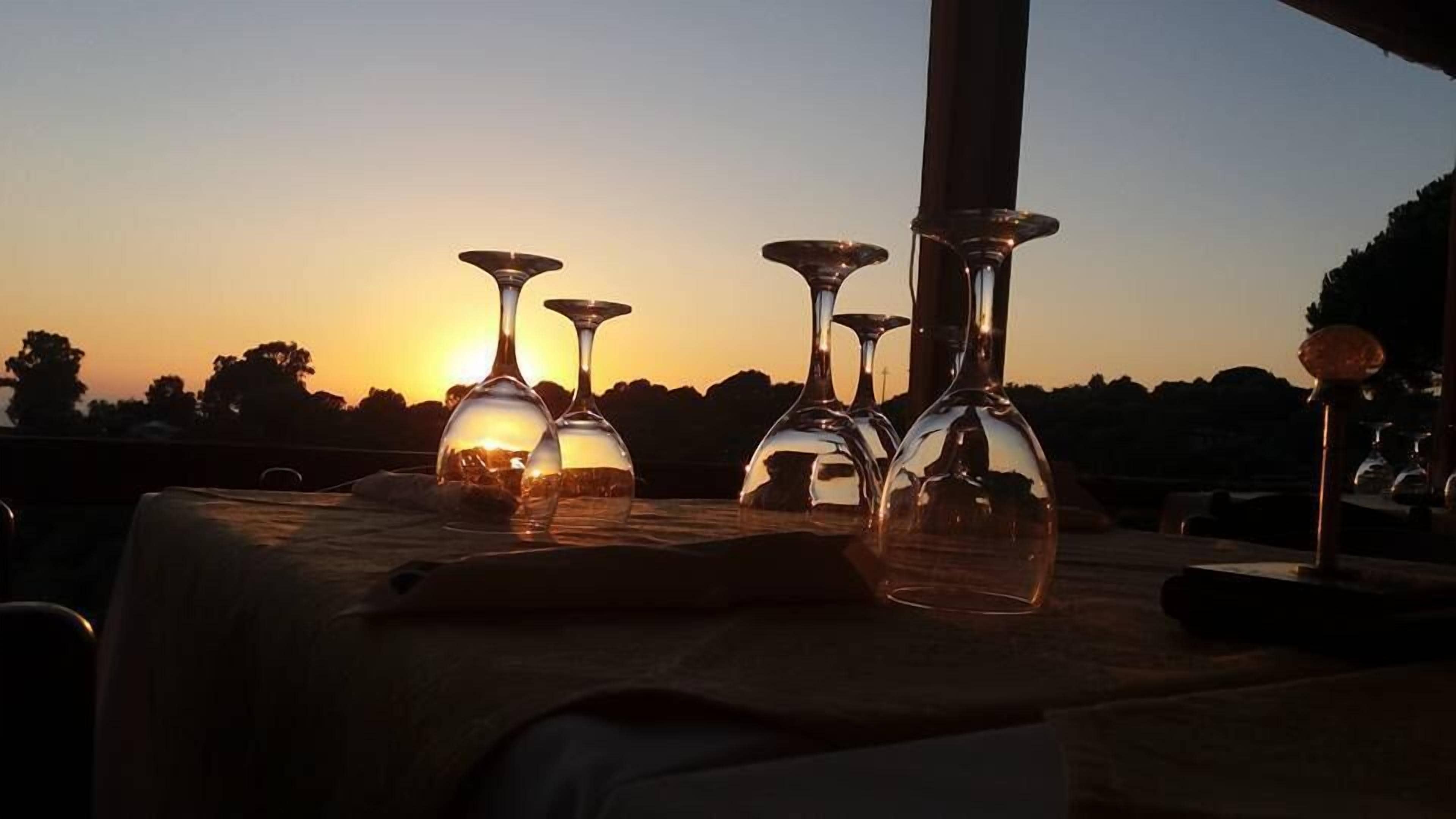Mesa com copos de vinho e uma garrafa, ao pôr do sol.