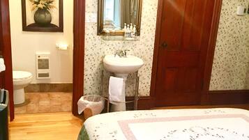 Quarto com uma cama grande, porta de madeira, espelho, pia e vaso sanitário.