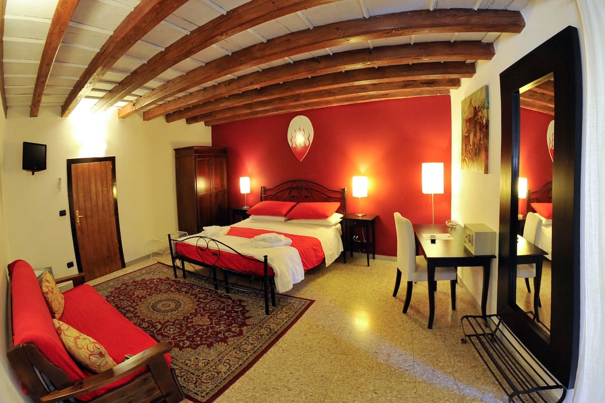 Quarto com cama, escrivaninha, cadeira, televisão e espelho.