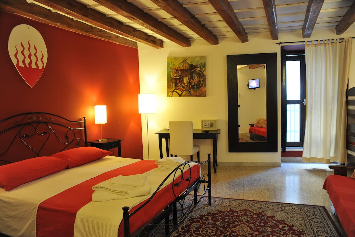Quarto de hotel com cama, escrivaninha, cadeira, luminária e um quadro na parede.
