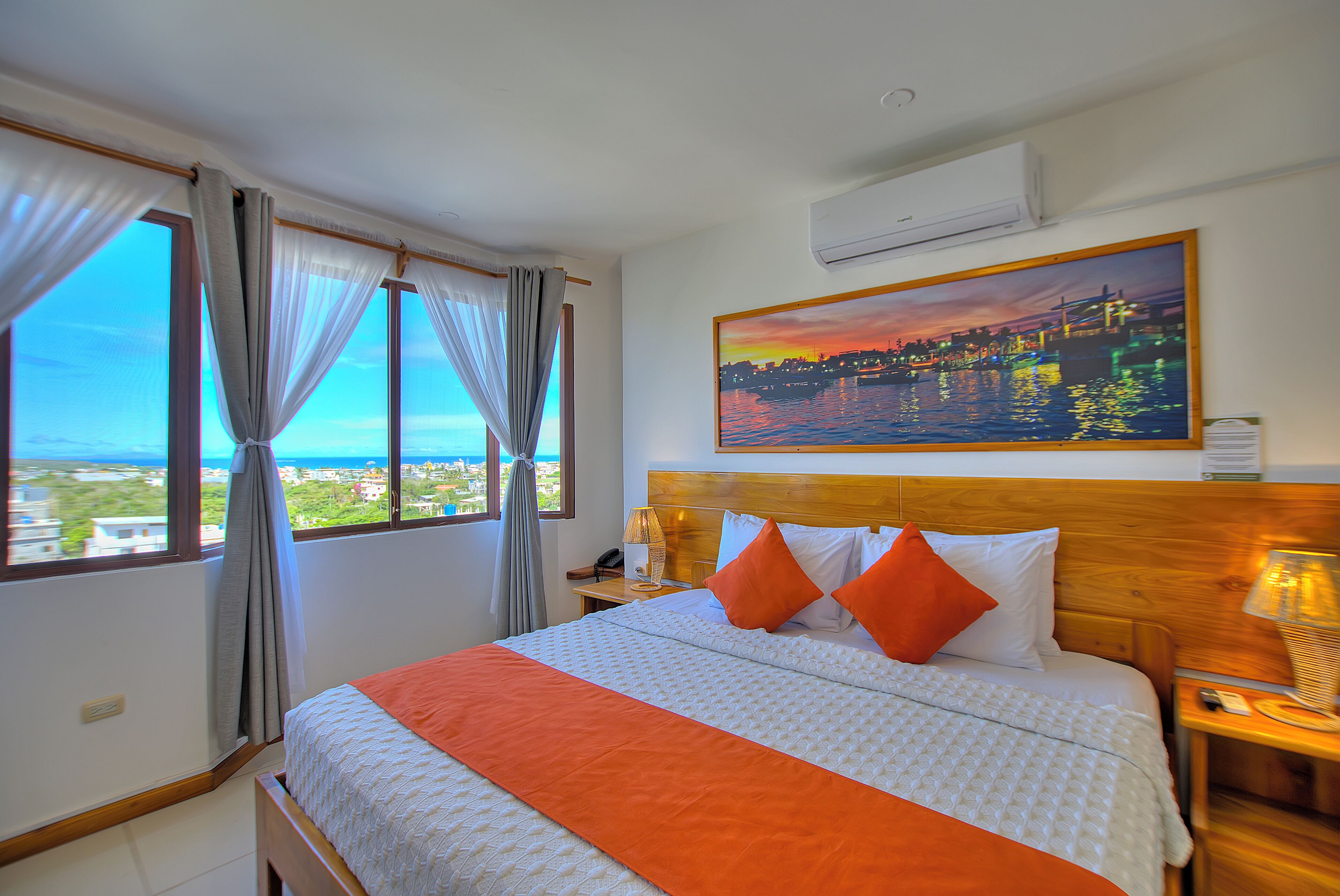 Quarto de hotel com uma cama grande, um quadro de uma paisagem urbana e vista para a cidade pela janela.