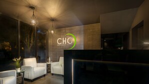 Uma área de recepção moderna com divisória de vidro, balcão de atendimento e duas poltronas brancas.