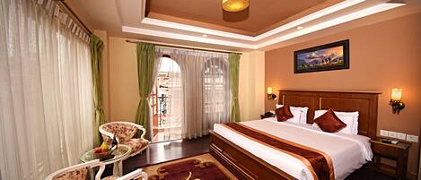 Quarto de hotel com uma cama grande, um espaço de estar com mesa e cadeiras, e vista para o exterior através de uma janela.