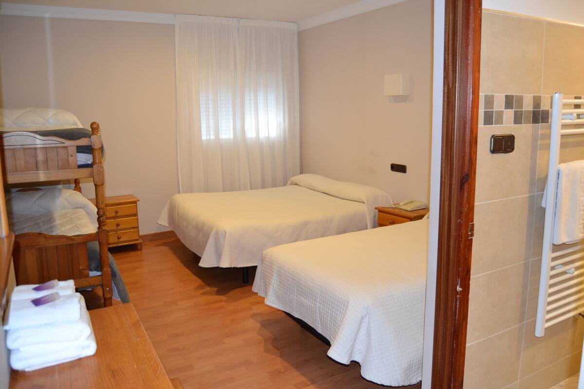 Quarto de hotel com duas camas, um guarda-roupa de madeira, uma mesa de cabeceira e área de chuveiro.