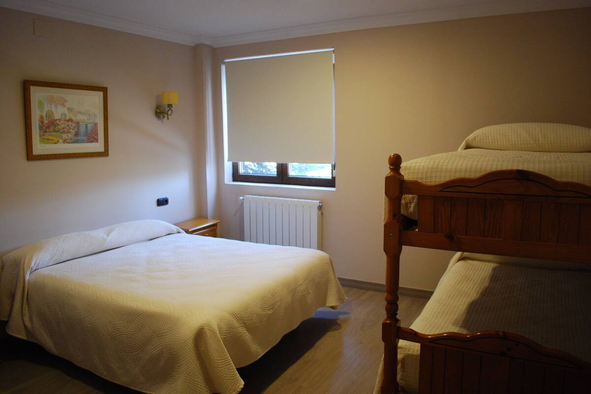 Quarto com uma cama de solteiro, uma janela com cortina, um radiador e um quadro na parede.