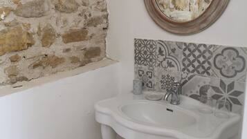 Casa de banho com parede de pedra, pia branca e azulejos estampados.