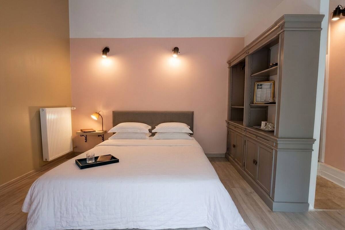 Uma cama bem arrumada com uma bandeja, uma mesinha de cabeceira com abajur e um armário embutido.