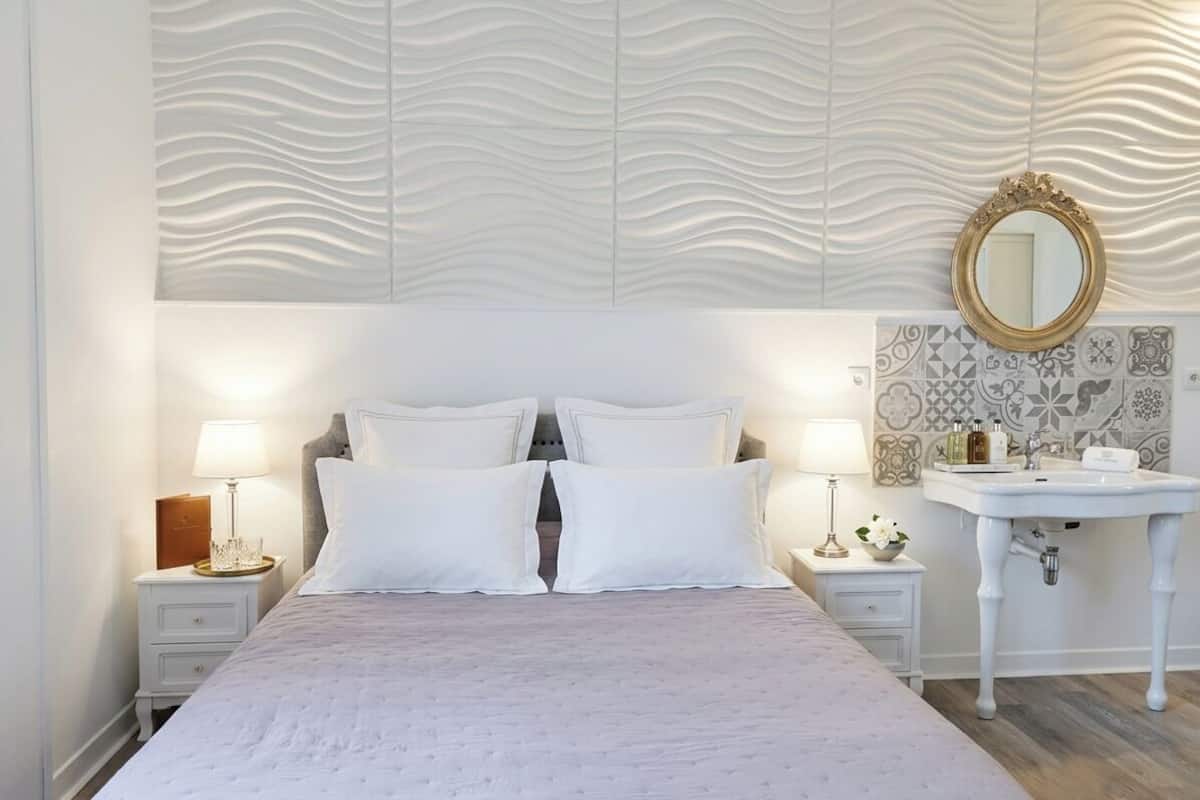 Quarto bem organizado com cama, duas mesas de cabeceira, um criado-mudo, espelho e pia de banheiro.