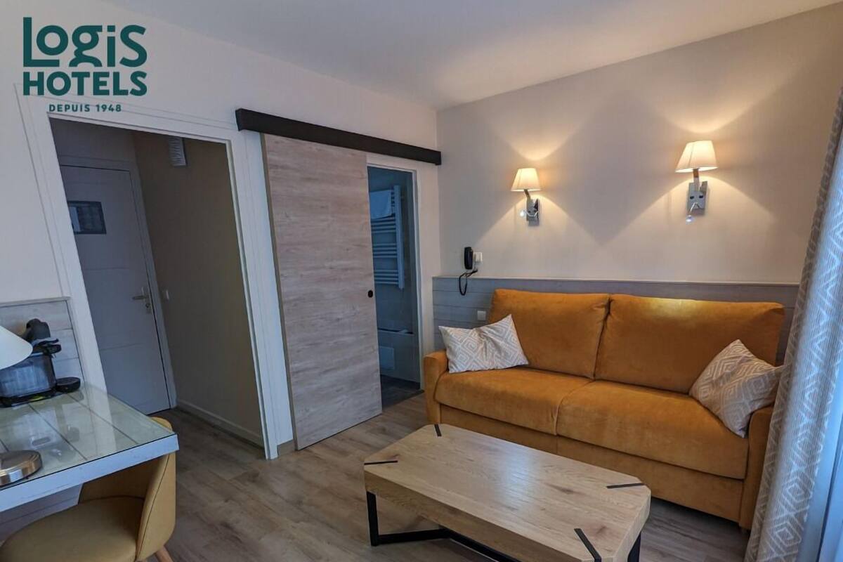 Uma sala de estar moderna com sofá, mesa de centro, escrivaninha e guarda-roupa. Há duas luminárias fixadas na parede.