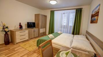 Quarto de hotel com cama, escrivaninha, televisão, guarda-roupa e janela com cortinas.