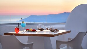 Uma mesa com bebidas e petiscos, com vista para montanhas e o mar.