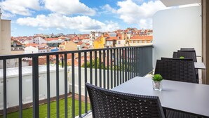 Varanda com mesa e cadeiras, vista para paisagem urbana com edifícios de telhado vermelho.