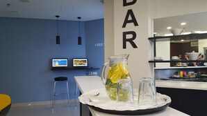 Uma área de bar com um jarro de água aromatizada com frutas, uma bandeja com copos e duas televisões na parede.