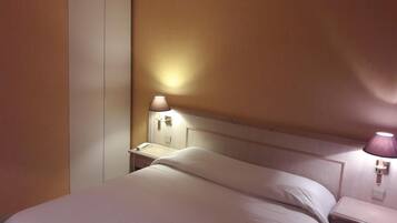 Quarto de hotel com cama, mesas de cabeceira e luminárias fixadas na parede.