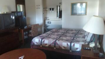 Quarto de hotel com cama, escrivaninha, cadeira, televisão e abajur.