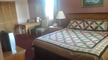 Quarto de hotel com cama, escrivaninha, cadeira, luminária e televisão.