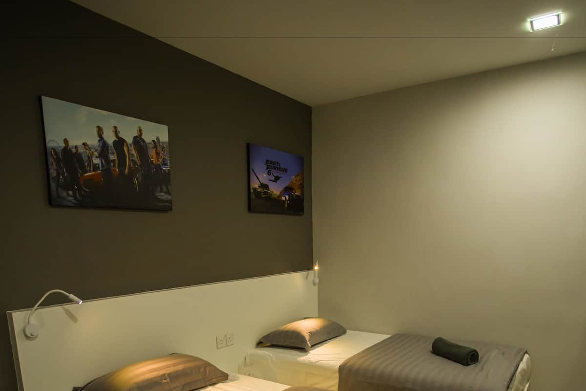 Quarto de hotel com duas camas, cabeceira, quadro na parede e iluminação no teto.