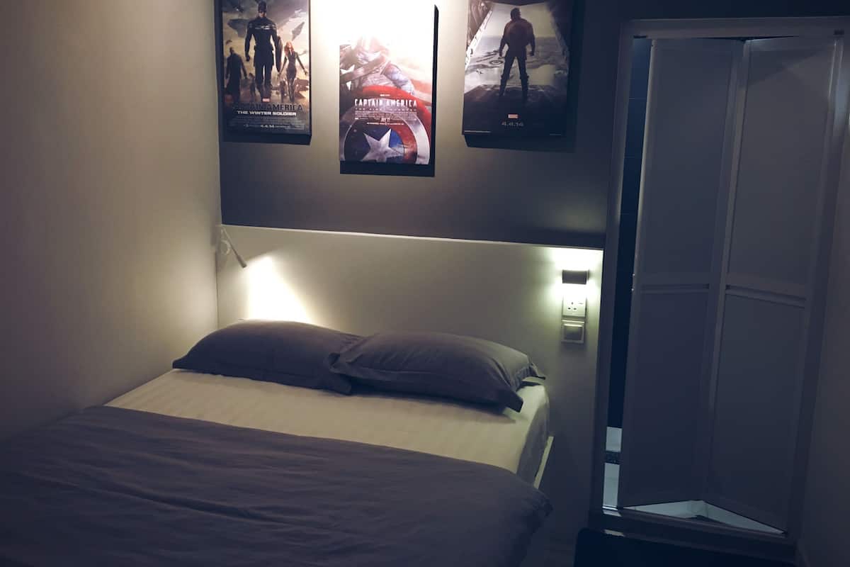 Quarto de hotel com cama, mesa de cabeceira e três cartazes de filmes na parede.