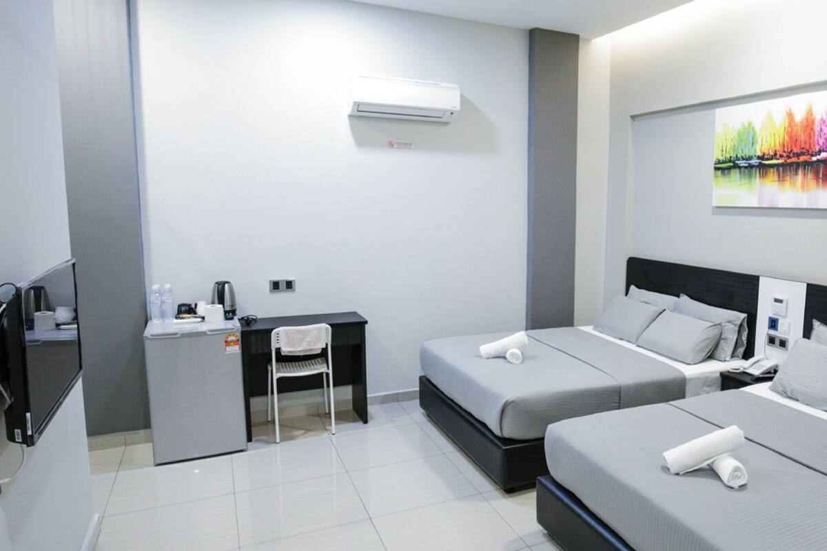 Quarto de hotel com duas camas, uma escrivaninha, uma cadeira, uma televisão e um quadro na parede.