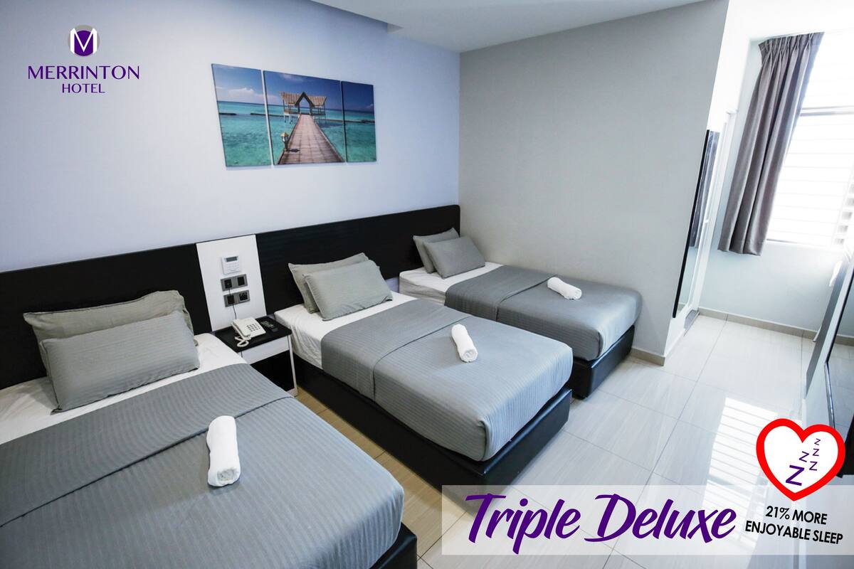 Quarto de hotel com três camas, um quadro de um cais e um aviso indicando um sono 21% mais agradável.