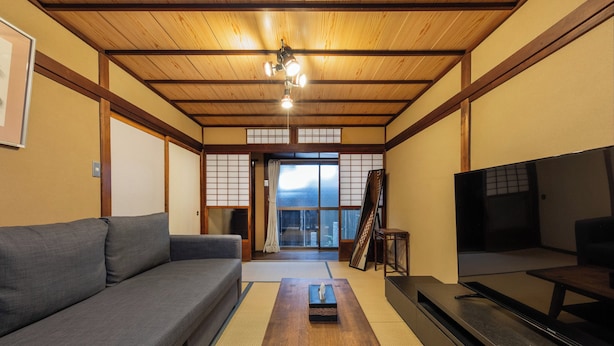 Uma sala de estar japonesa tradicional com tatames, uma mesa de madeira baixa, um sofá e uma televisão.