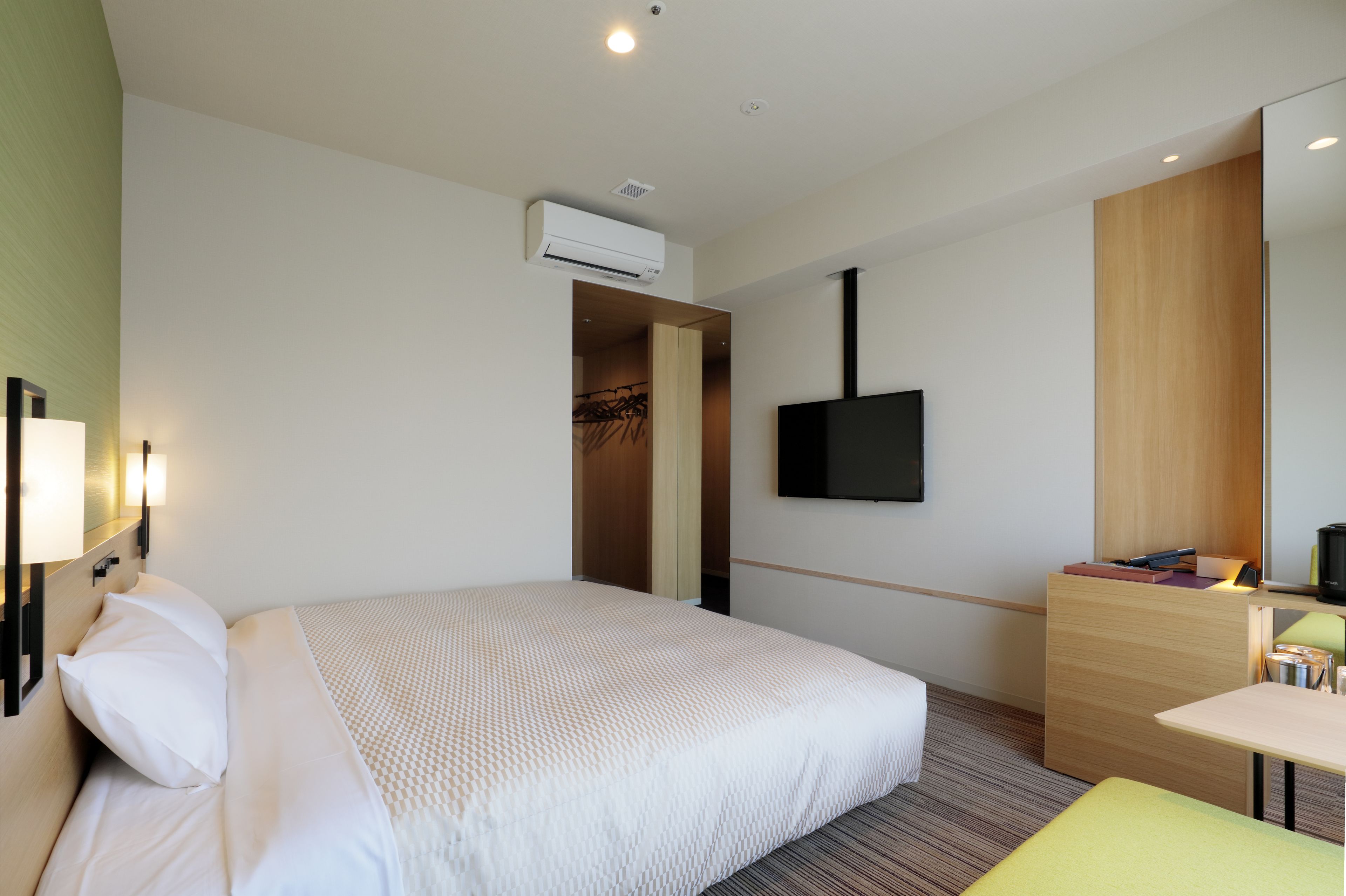 Quarto de hotel com cama, mesa de cabeceira, televisão fixada na parede e aparelho de ar condicionado.