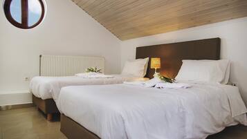 Quarto de hotel com duas camas, teto de madeira, radiador e uma pequena janela.