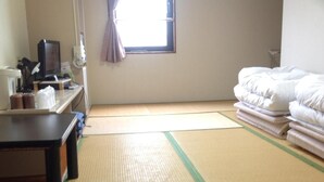 Quarto com tatames, cama com roupa de cama branca, escrivaninha com computador e janela com cortinas.