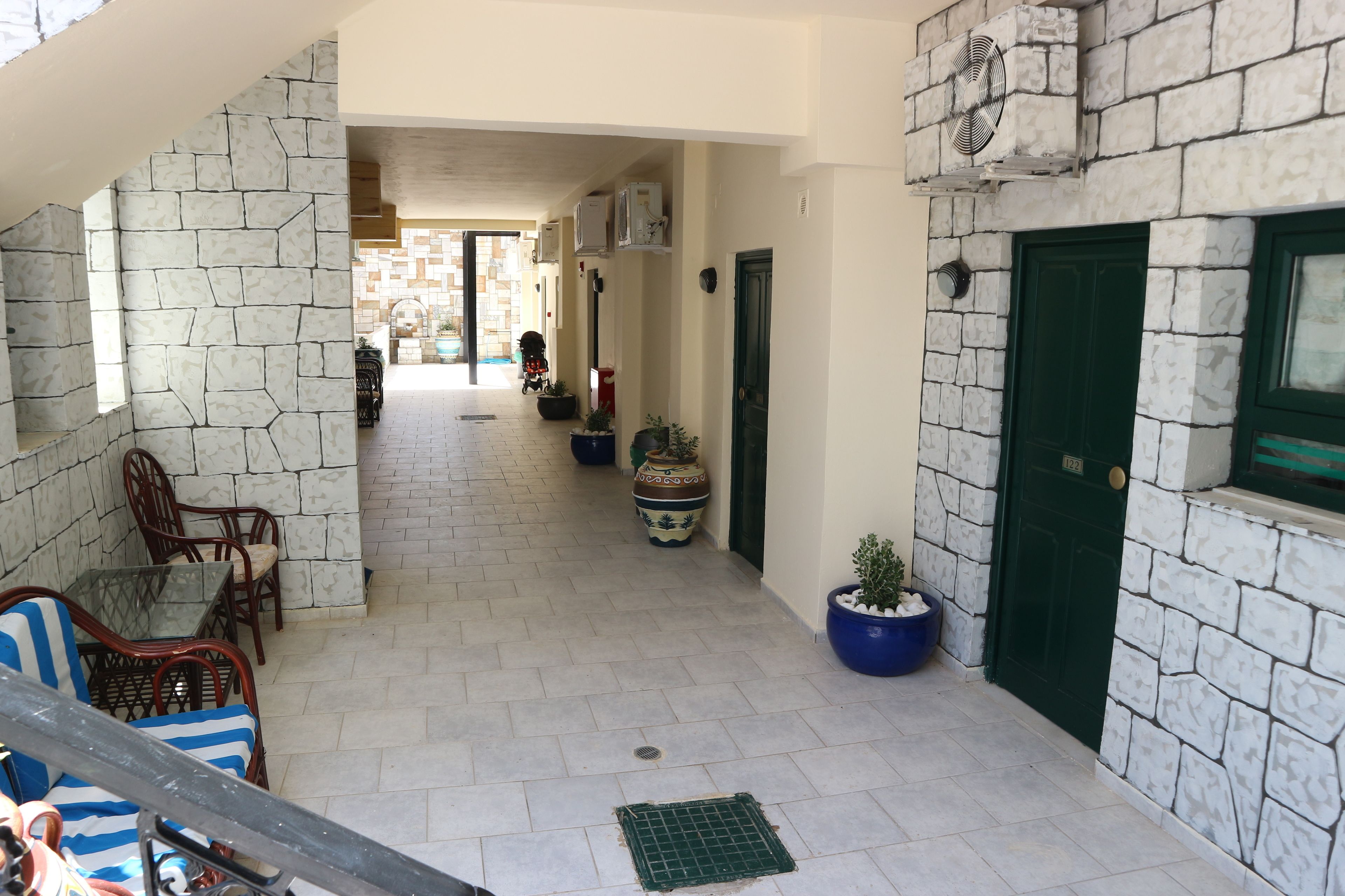 Um corredor com paredes de pedra, uma porta verde e plantas em vasos.