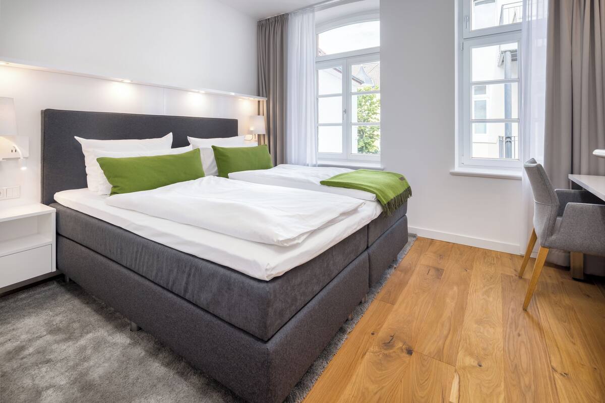 Quarto de hotel moderno com uma cama grande, uma escrivaninha e uma janela com cortinas.
