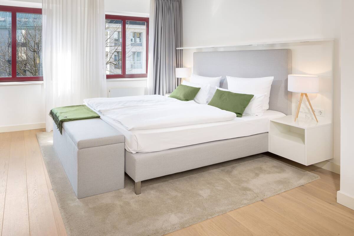 Quarto moderno com uma cama grande, mesas de cabeceira e vista da cidade através de amplas janelas.
