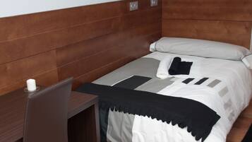 Cama bem arrumada com cabeceira, mesa de cabeceira com abajur e pequena mesa com vela.