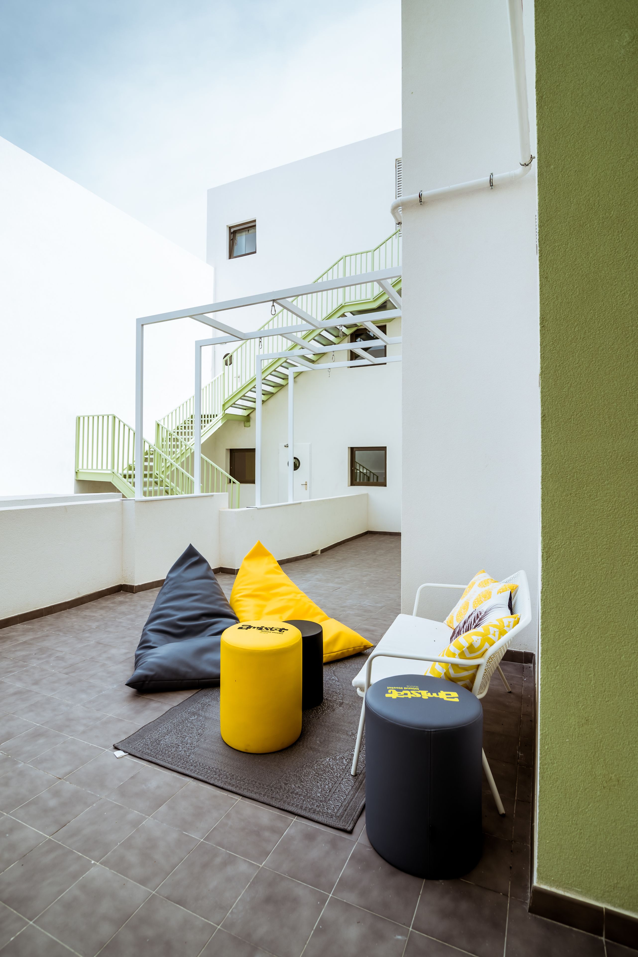 Terraço no telhado com parede branca, escadaria verde e um banquinho amarelo e preto.