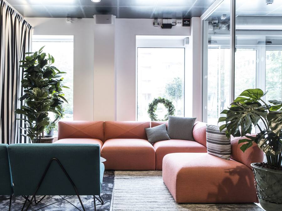 Uma sala de estar moderna com sofá em forma de L, poltronas verde-água e plantas em vasos.